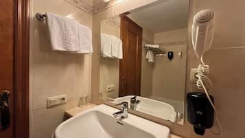 Casa de banho com lavatório branco, espelho, suporte para toalhas, secador de cabelo e dispensador de toalhas.