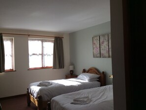 Quarto com duas camas de solteiro, uma janela com cortinas, mesa de cabeceira com abajur e uma obra de arte floral na parede.