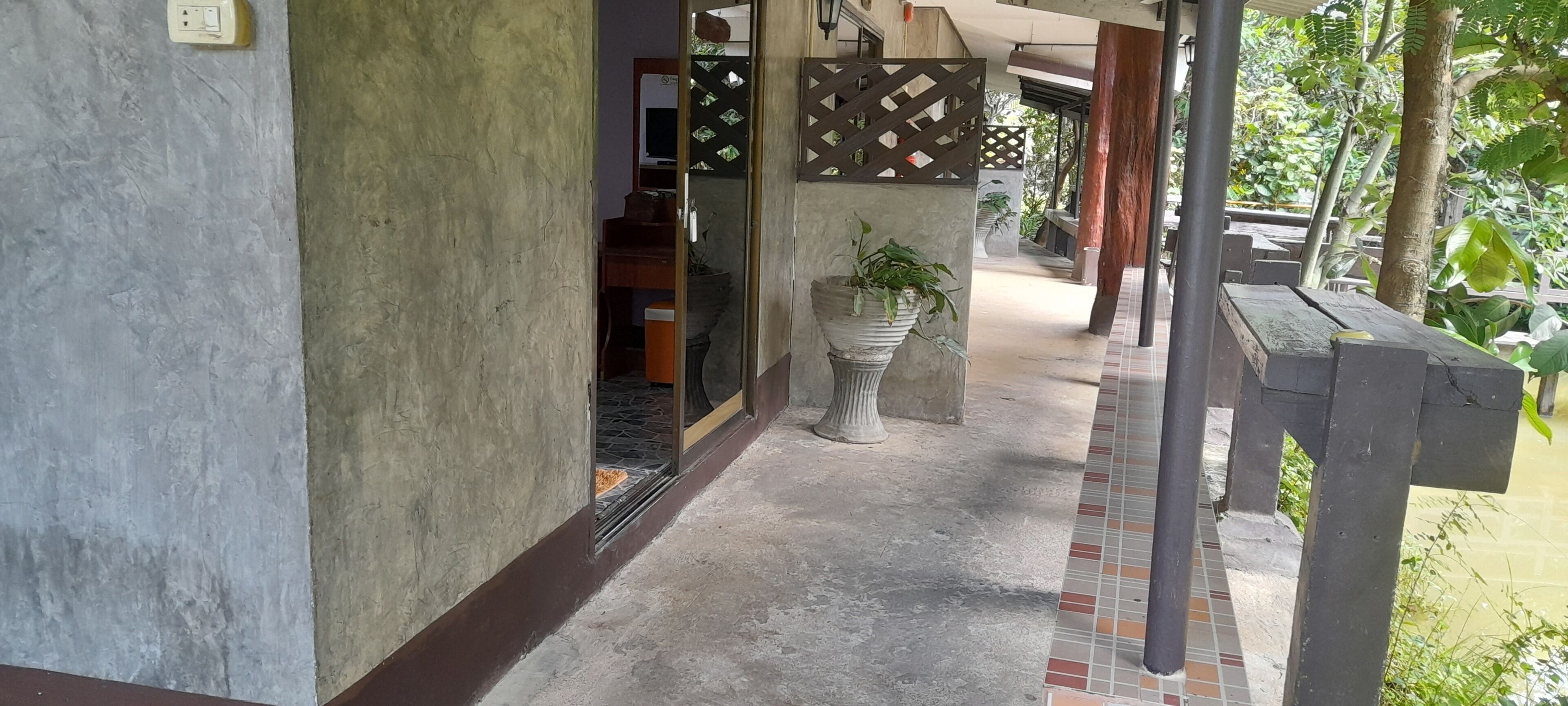 Uma área externa coberta com piso de concreto, um vaso de planta e um banco de madeira.