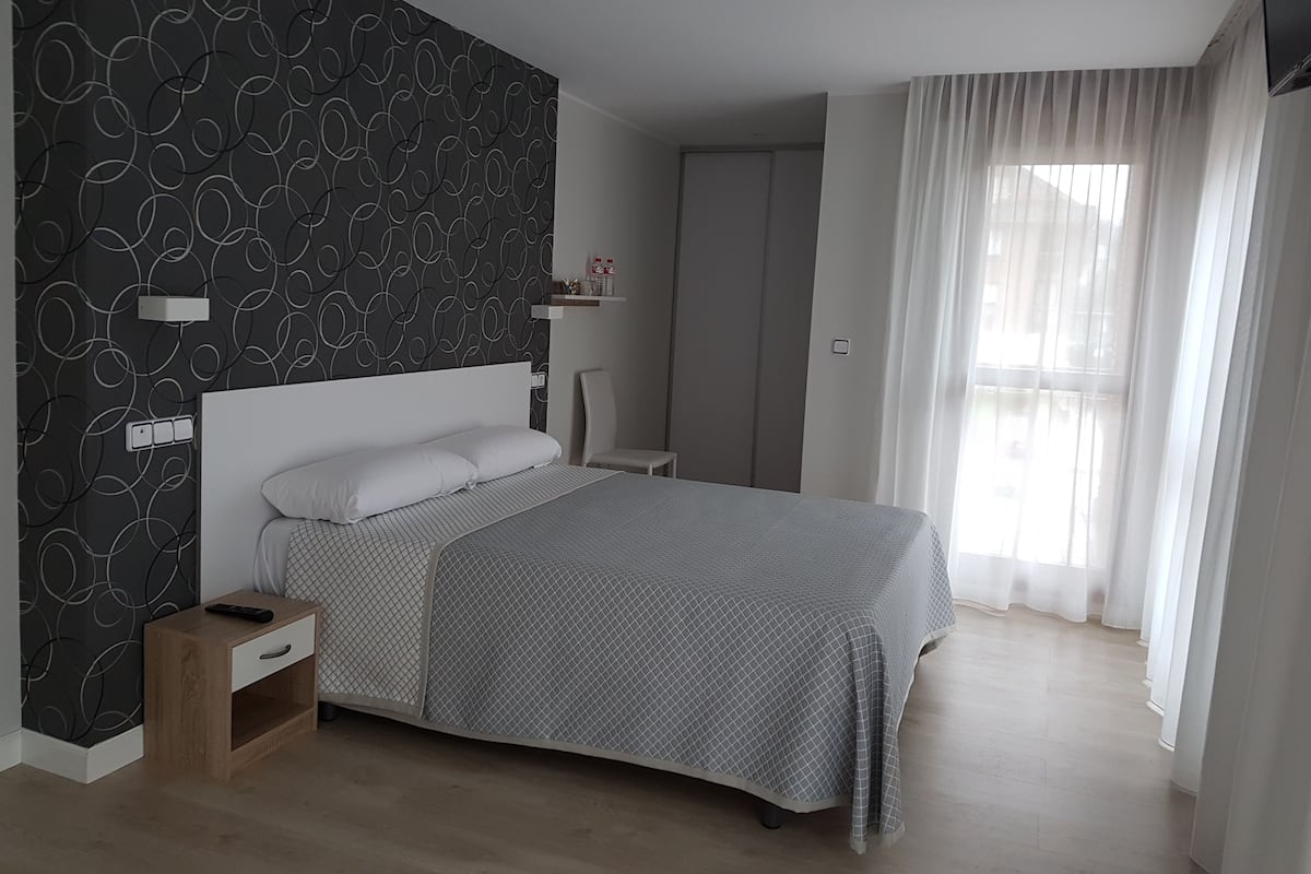 Quarto moderno com cama, mesa de cabeceira, guarda-roupa e janela com cortinas.