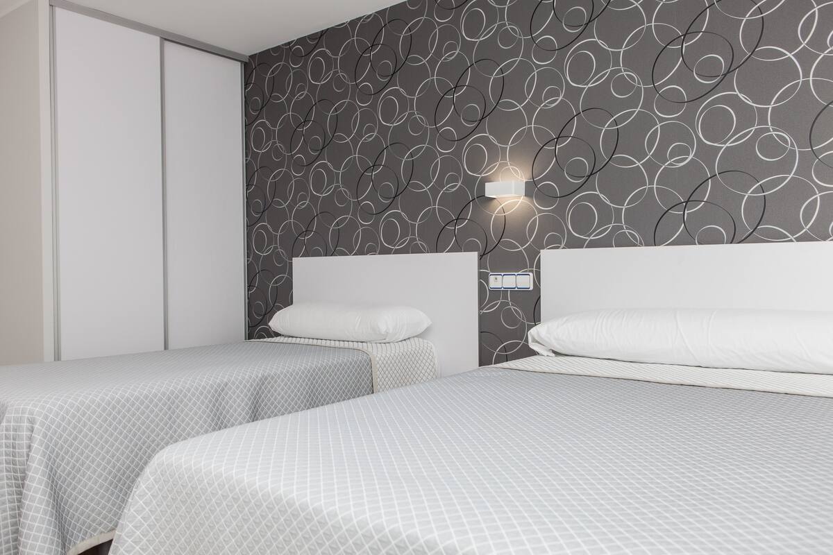 Quarto de hotel com duas camas de solteiro, um guarda-roupa e uma parede com padrão circular.