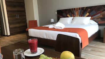 Quarto de hotel com uma cama, mesa de cabeceira, abajur, cesta de frutas e um copo de suco.