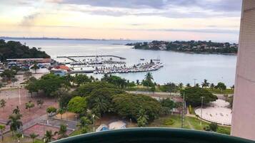 Uma marina com barcos atracados, uma vasta extensão de água e uma linha costeira distante com edifícios.