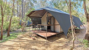 Uma tenda com um deck de madeira e uma mesa, cercada por árvores.