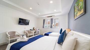 Quarto de hotel com duas camas, uma escrivaninha, cadeiras, televisão e um quadro na parede.