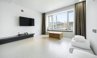 Quarto de hotel moderno com uma janela grande, televisão de tela plana na parede, um banco de madeira e um sofá branco.