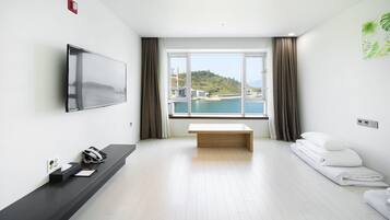 Quarto de hotel com uma janela grande, uma cama, uma mesa de cabeceira com telefone e uma televisão de tela plana na parede.