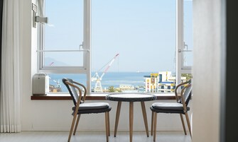 Quarto com duas cadeiras viradas para uma janela grande com vista para uma área de construção e um corpo de água.