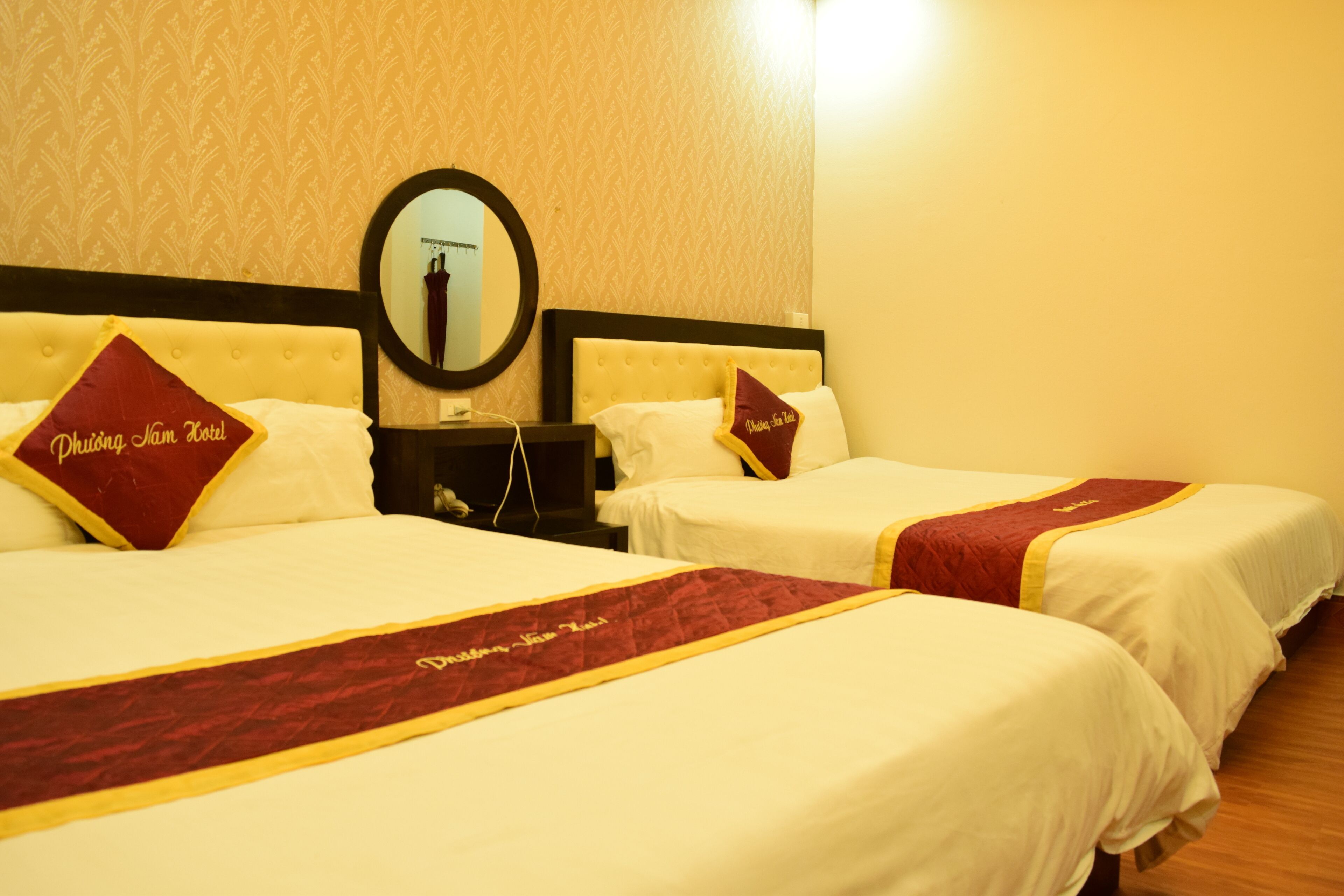 Quarto de hotel com duas camas, cada uma com colcha e almofadas vermelhas e brancas. Há um espelho redondo na parede acima das camas.