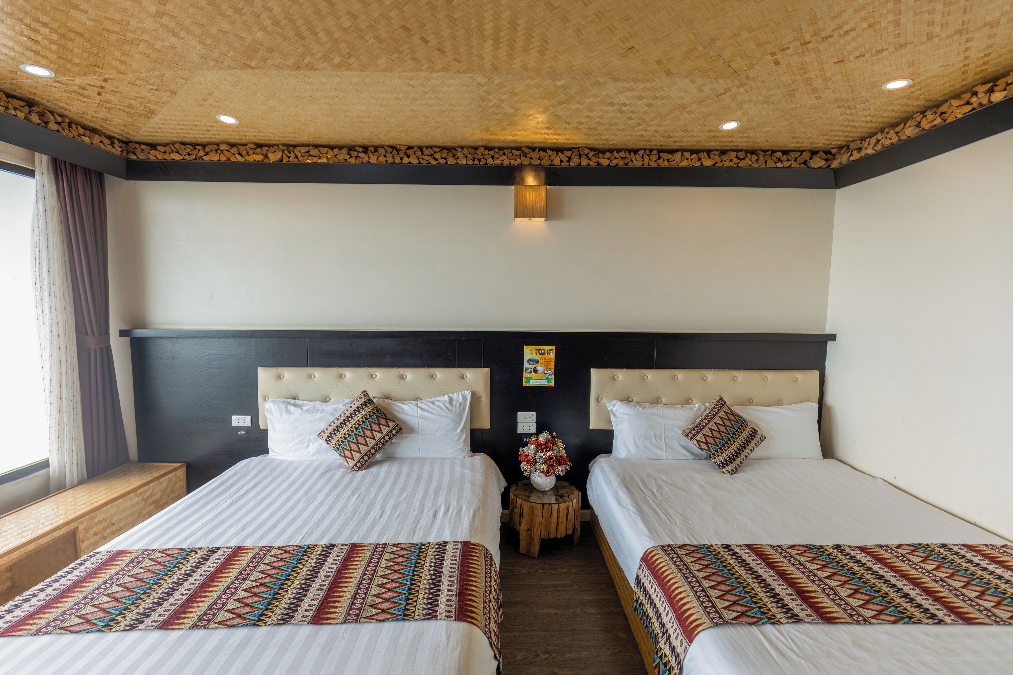 Quarto de hotel com duas camas, teto de madeira e uma pequena mesa redonda com um vaso de flores.