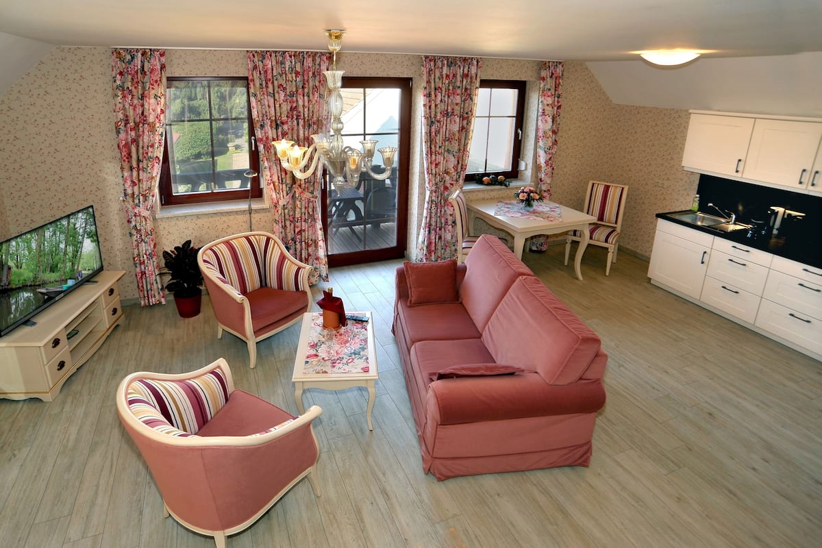 Uma sala de estar com sofá, poltrona, TV e área de refeições com mesa e cadeiras.