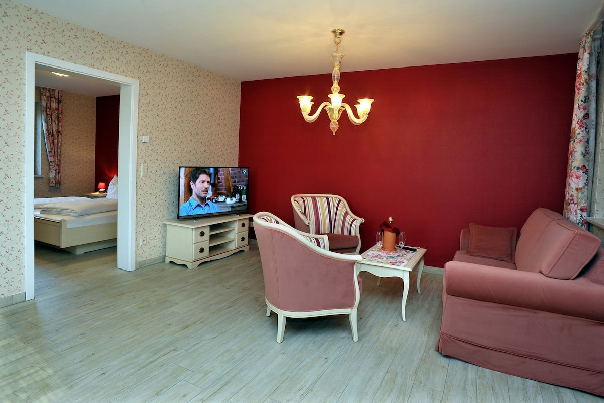 Uma sala de estar com televisão, sofá, poltrona e mesa.