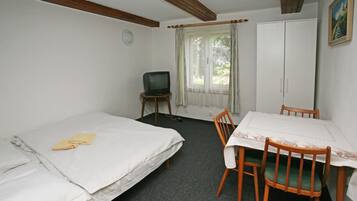 Quarto com cama, mesa e cadeiras, televisão sobre uma mesinha e janela com cortinas.