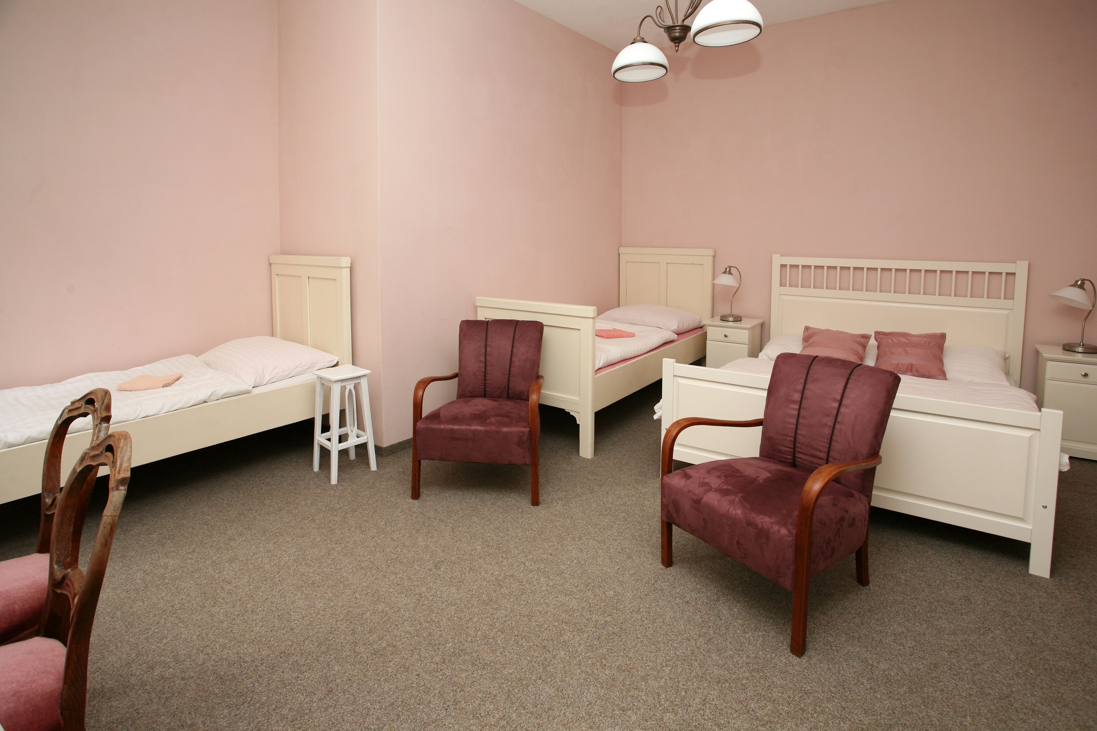 Quarto com duas camas de solteiro, duas cadeiras de madeira, uma mesinha de cabeceira e um abajur.