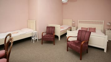 Quarto com duas camas de solteiro, duas cadeiras de madeira, uma mesinha de cabeceira e um abajur.