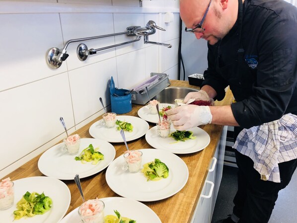 Um chef prepara pratos com legumes e frutos do mar em uma bancada de cozinha.