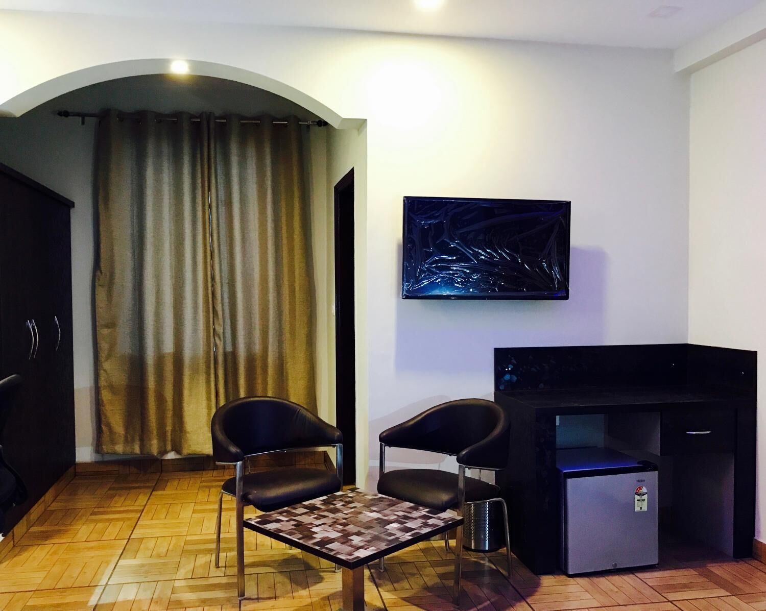Um espaço de estar compacto com sofá, duas cadeiras, uma mesinha, televisão e mini-geladeira.