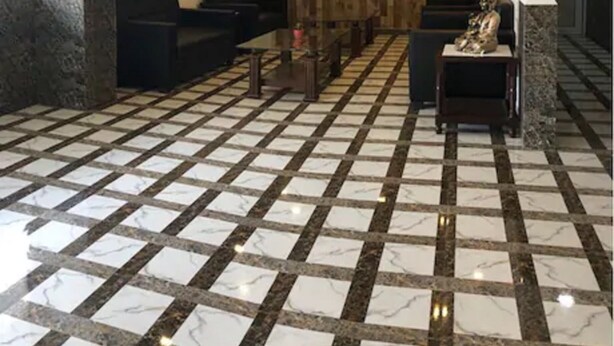 Um hall com piso de mármore quadriculado, área de estar com sofás, uma televisão fixada na parede e um aparelho de ar condicionado.