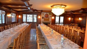 Uma longa mesa de jantar posta com cadeiras, um candelabro e uma lareira ao fundo.
