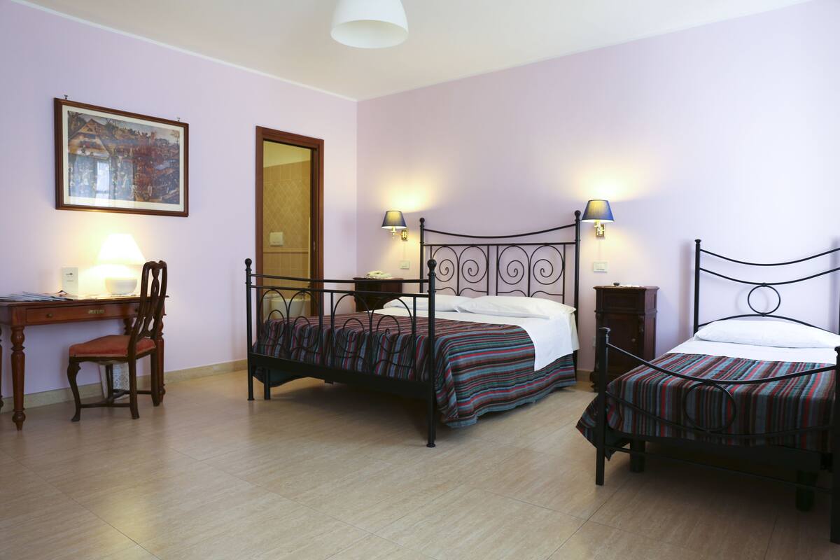 Quarto com duas camas, uma escrivaninha e uma cadeira.