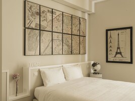Um quarto com um grande mapa de Paris, uma ilustração emoldurada da Torre Eiffel, um globo em uma mesa de cabeceira e um letreiro com a palavra 'LOVE' na cabeceira.