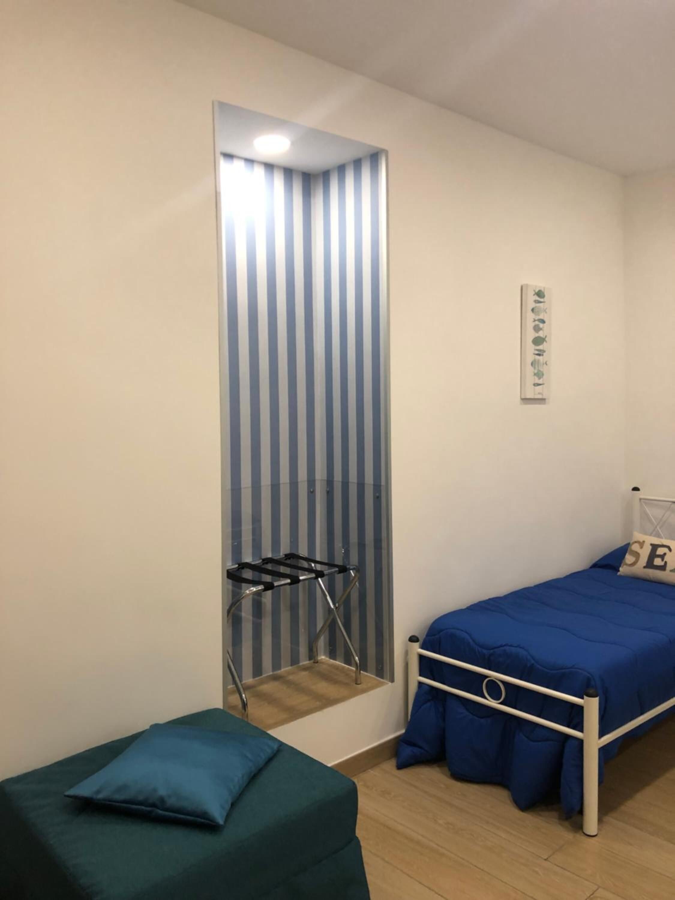 Quarto pequeno e bem organizado, com uma cama, uma cadeira e uma mesinha.