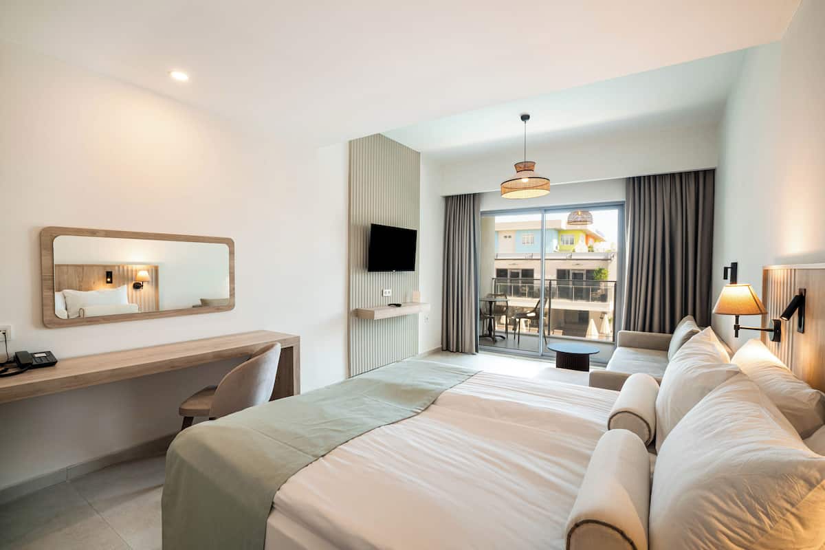 Quarto de hotel com cama grande, escrivaninha com cadeira, televisão fixada na parede e varanda com vista externa.