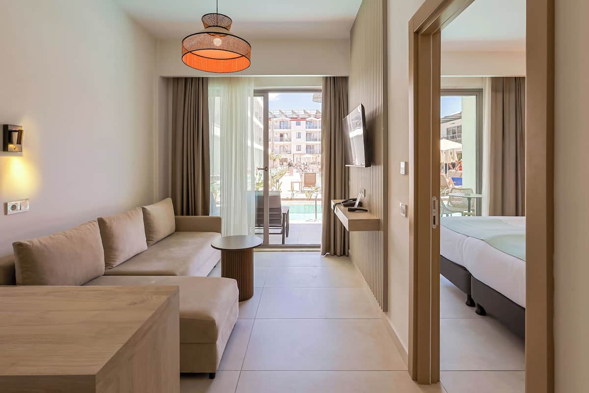 Quarto de hotel com sofá, mesa pequena, cama, televisão e vista para a área externa.