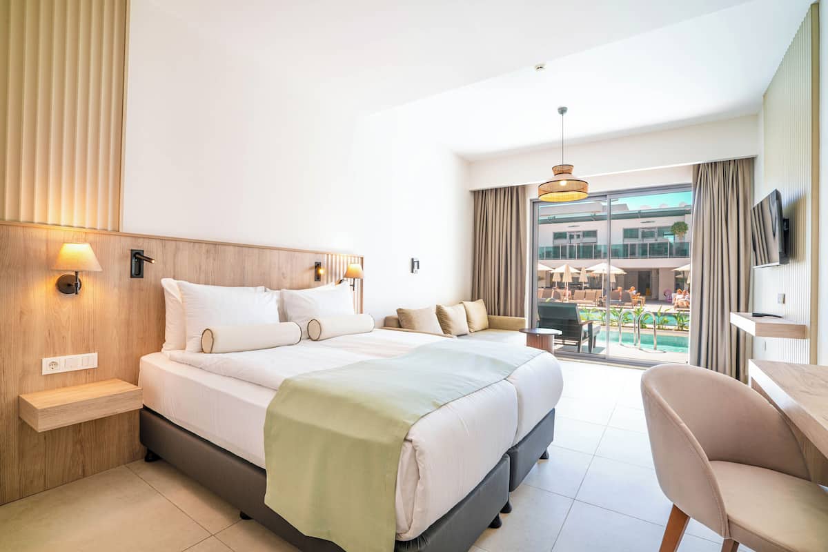 Quarto de hotel moderno com uma cama grande, uma escrivaninha e vista para a área da piscina.