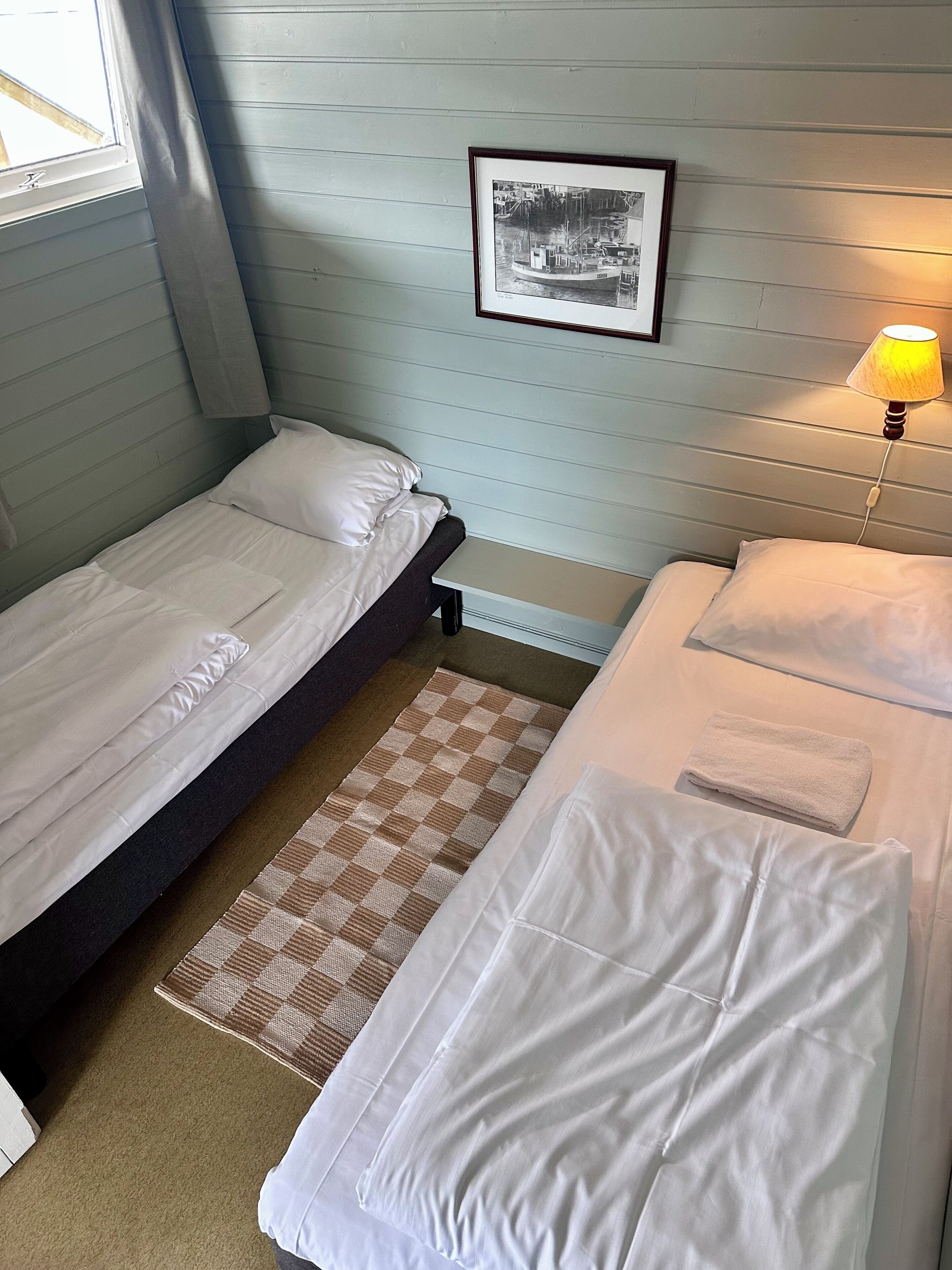 Quarto com duas camas, um tapete xadrez, um quadro na parede e um abajur.
