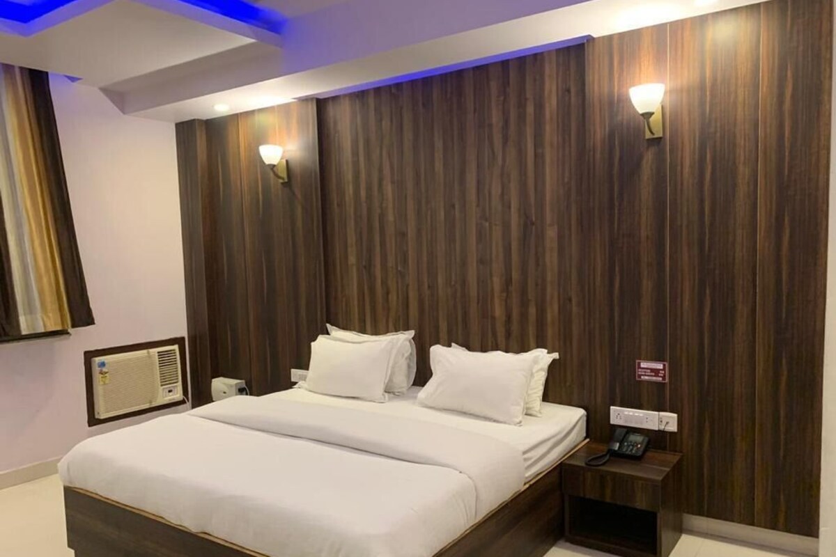 Quarto de hotel com uma cama grande, uma mesa de cabeceira com telefone e luminária na parede.