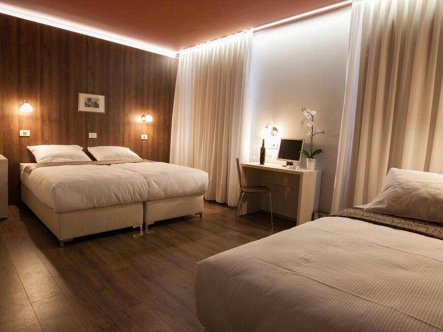 Quarto de hotel com parede de destaque em madeira, cama com roupa de cama branca, escrivaninha com computador e uma pequena planta em vaso.