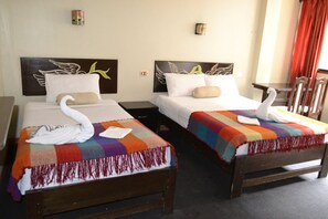 Duas camas de casal com almofadas decorativas em formato de cisne, um cobertor colorido e obras de arte nas paredes.