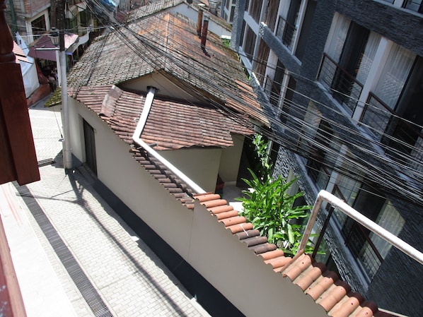Uma varanda estreita e elevada com telhado de azulejos, rodeada por edifícios urbanos densos e linhas de eletricidade.