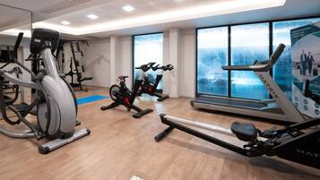 Uma academia com equipamentos de cardio, uma máquina de remo e uma janela ampla com vista para uma paisagem nevada.