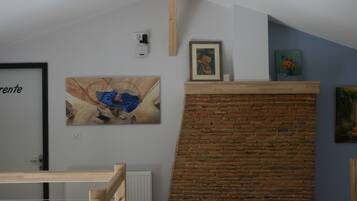Um quarto com parede de tijolos, escada de madeira e diversas obras de arte nas paredes.