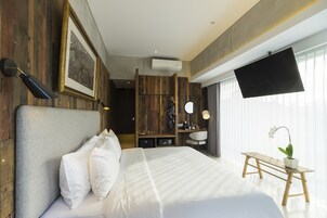 Quarto de hotel moderno com uma cama grande, uma escrivaninha, uma cadeira, uma televisão e uma janela com cortinas.