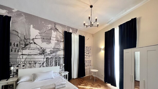 Um quarto com uma cama, uma mesinha de cabeceira, uma cadeira, um guarda-roupa e um mural na parede.
