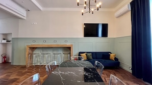 Uma sala de estar moderna com uma mesa de jantar, cadeiras transparentes, um sofá azul, lareira e uma televisão grande.