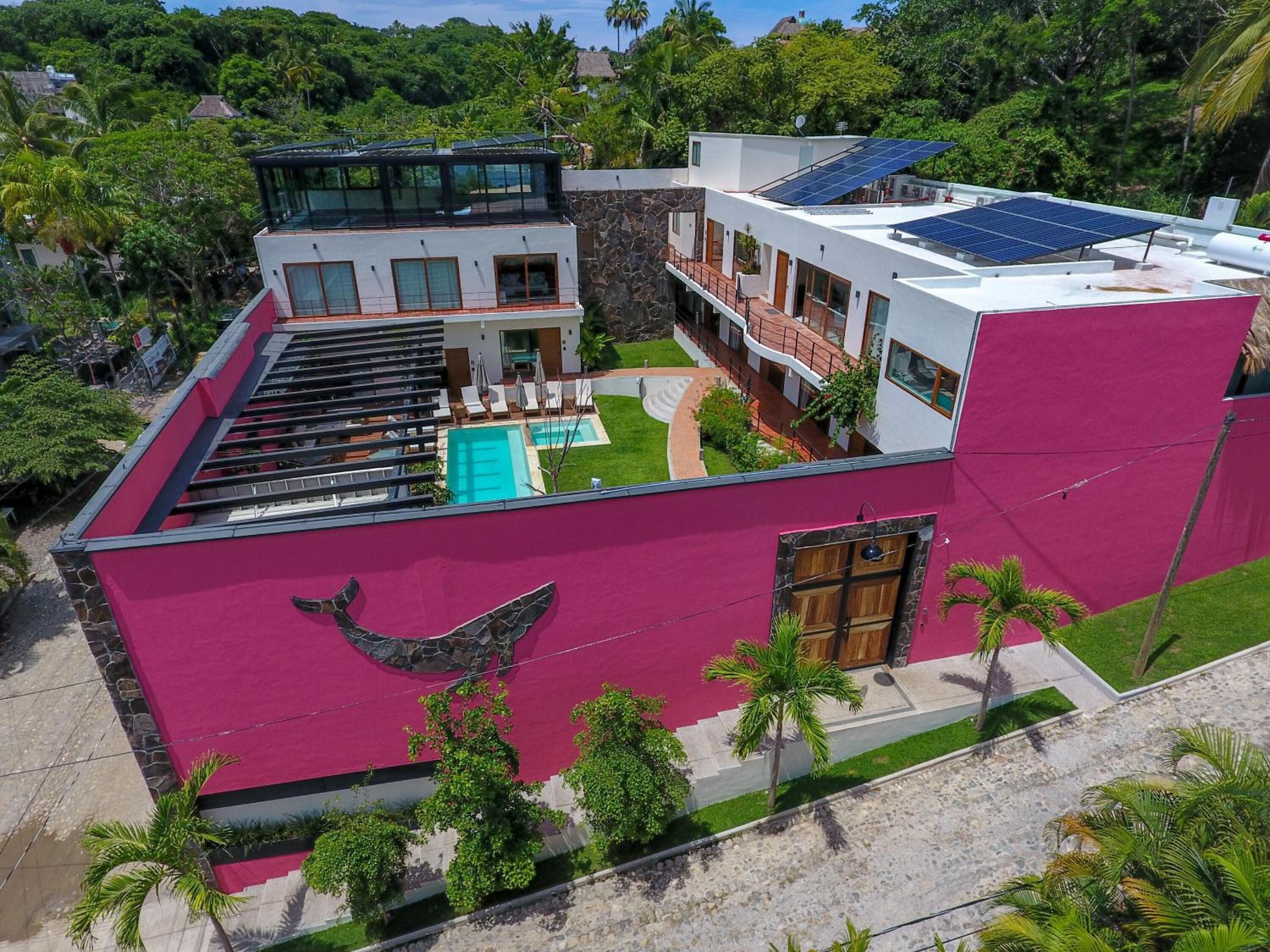 Um edifício moderno de vários andares com painéis solares, piscina e jardim tropical.