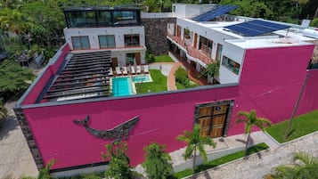 Um edifício moderno de vários andares com painéis solares, piscina e jardim tropical.