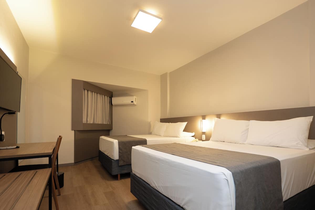Quarto de hotel com duas camas, uma escrivaninha e uma cadeira.