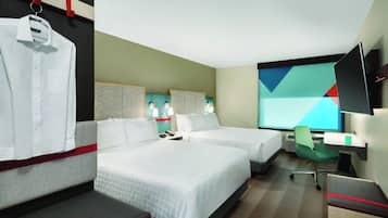 Quarto de hotel com duas camas, uma escrivaninha, uma cadeira, uma televisão e uma janela com vista geométrica.