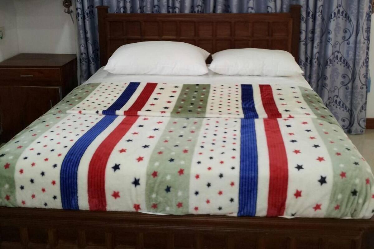 Uma cama com um cobreleiro estampado, uma cabeceira de madeira e uma cortina com padrão paisley.