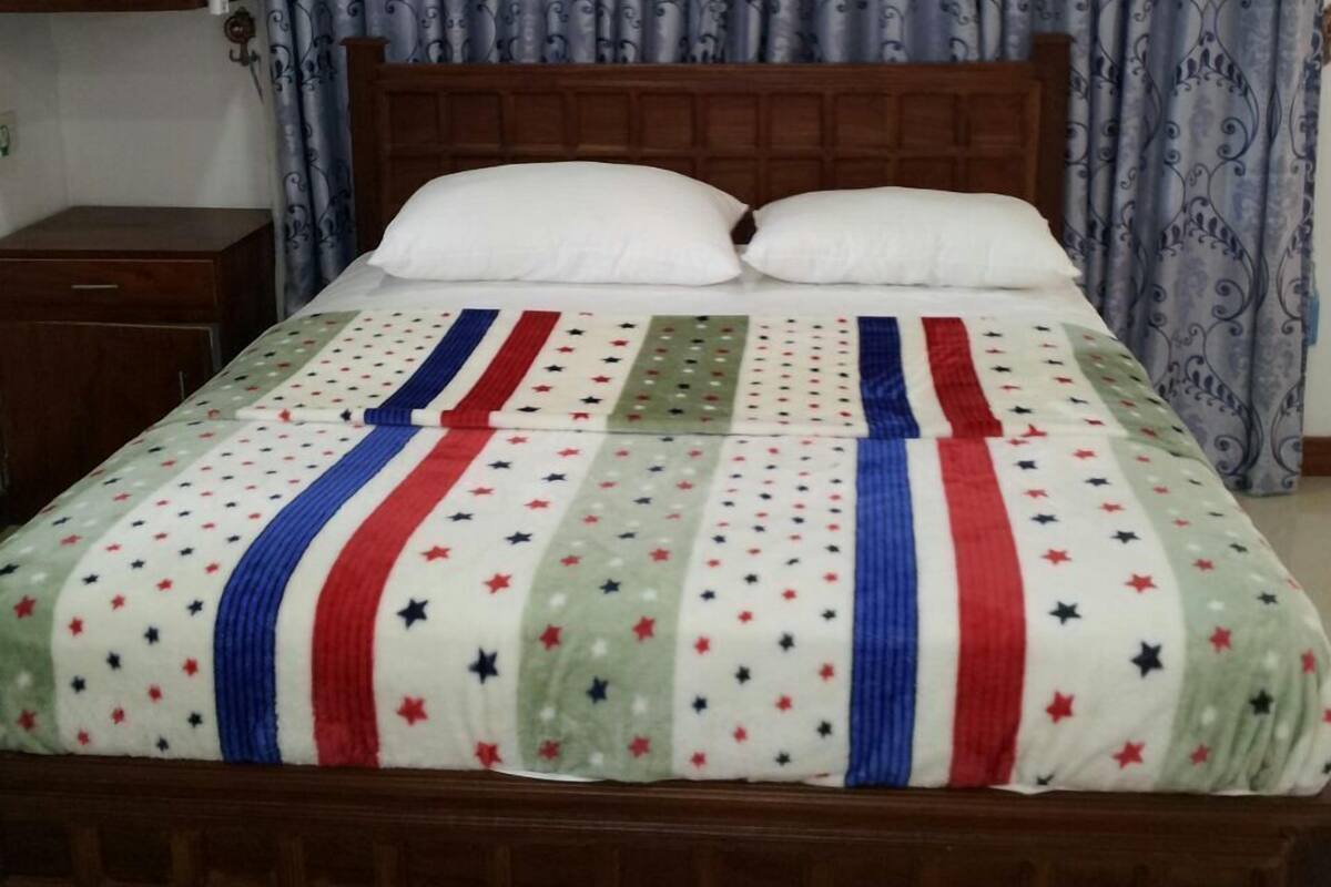Uma cama com colcha estampada, cabeceira de madeira e cortina com padrão paisley.