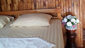 Quarto com paredes de madeira, uma cama, almofadas, uma mesinha de cabeceira e um vaso de flores.