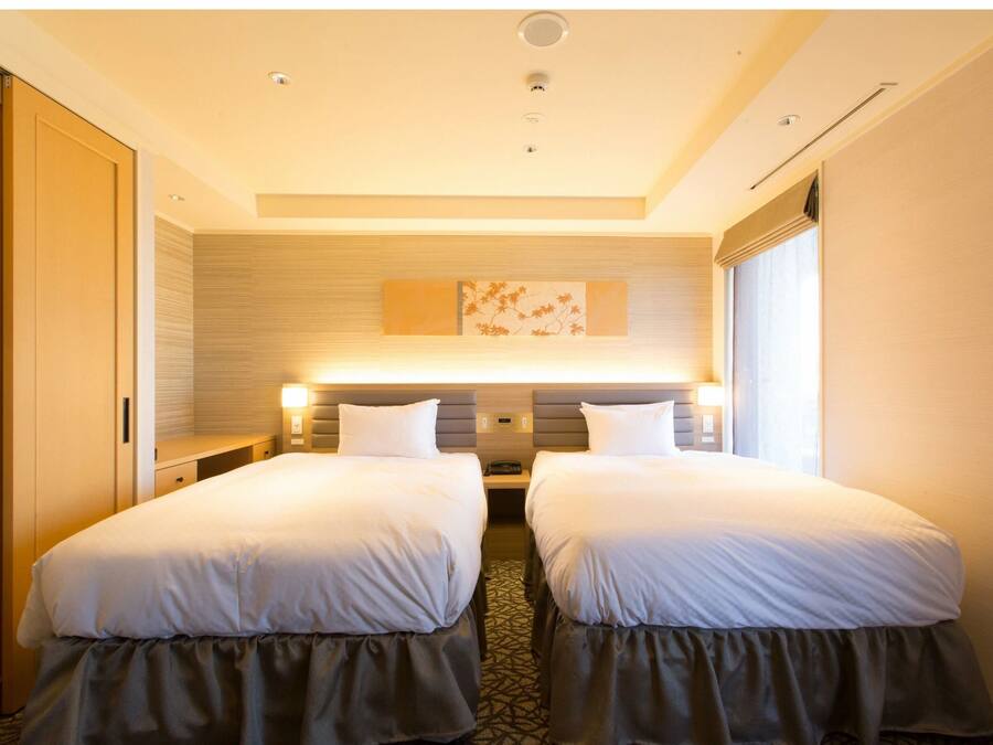 Quarto de hotel com duas camas, uma janela grande e uma obra de arte na parede.