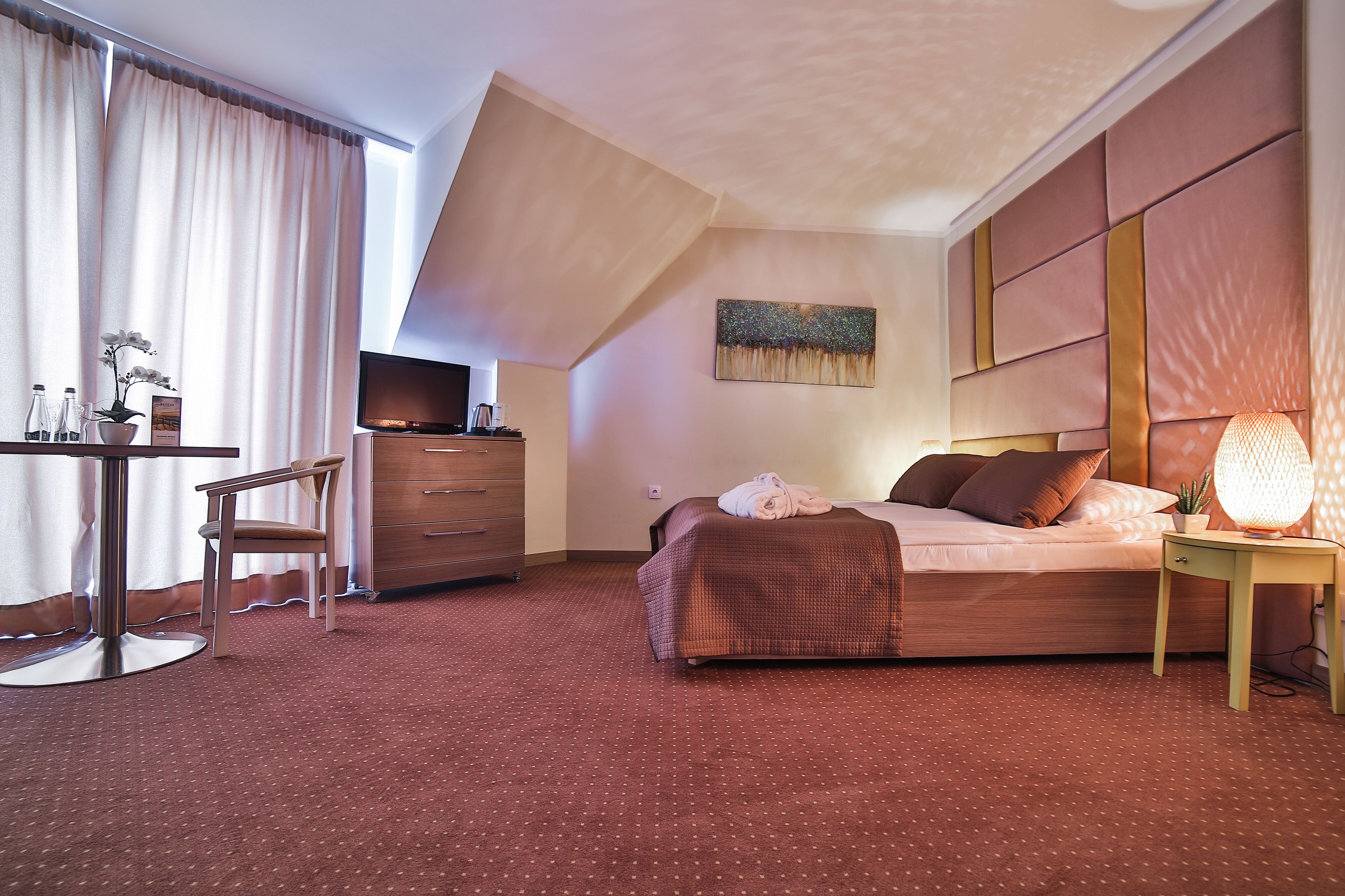 Quarto de hotel com cama, escrivaninha, cadeira, televisão e um quadro na parede.