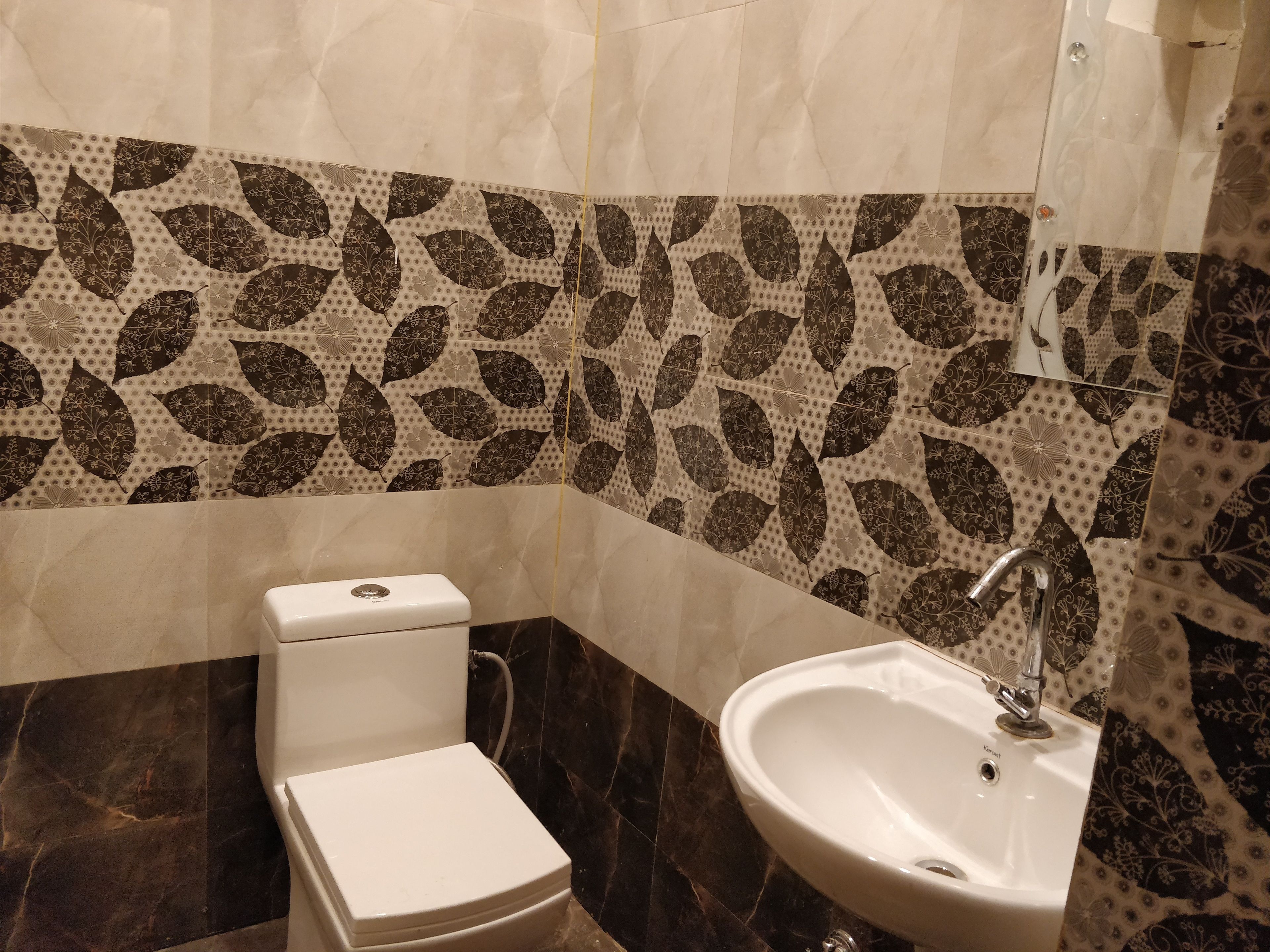 Casa de banho com sanita, lavatório e azulejos com padrão.