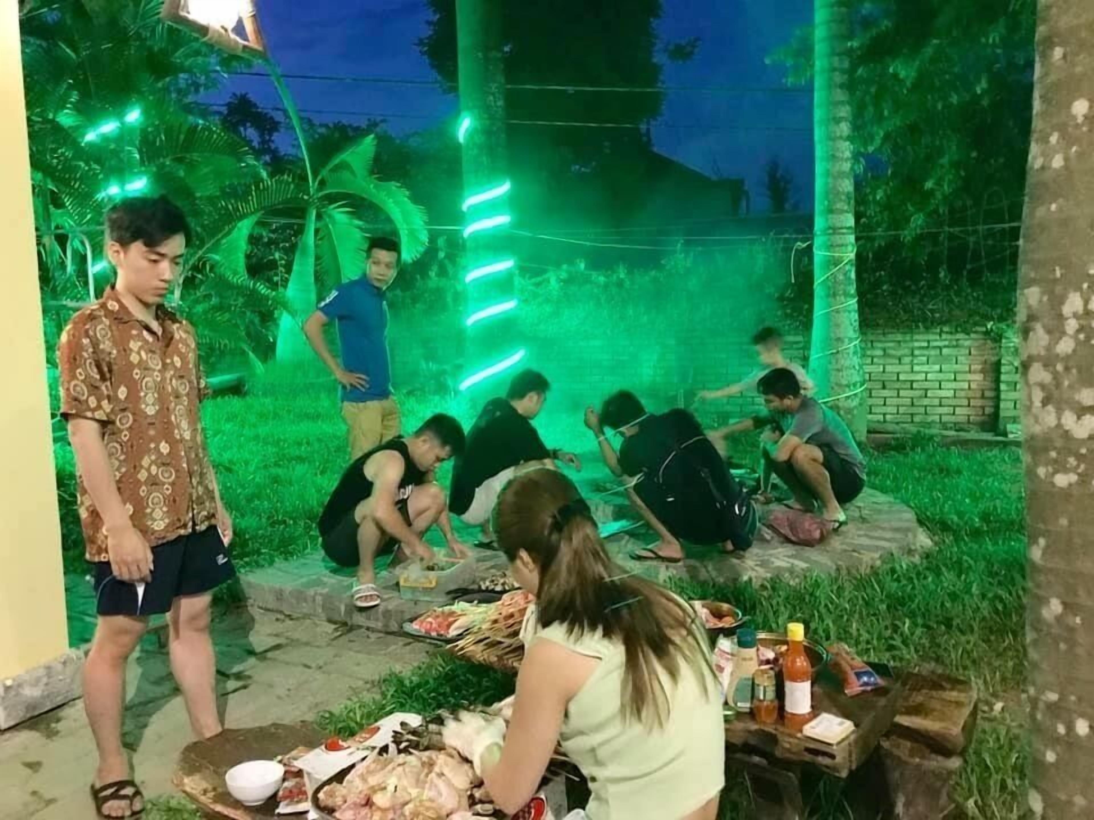 Um grupo de pessoas reunido em volta de uma mesa com comida e bebida, em ambiente externo com iluminação verde.